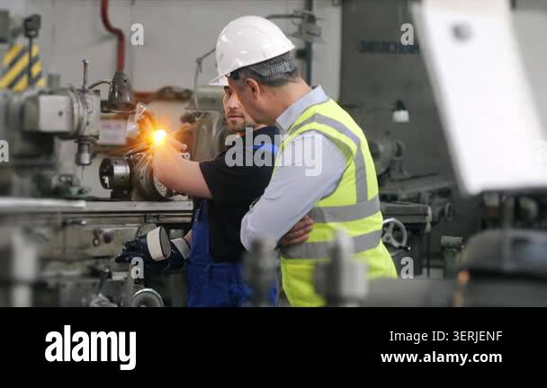 Industrial worker operating a metalworking machine while supervisor ...