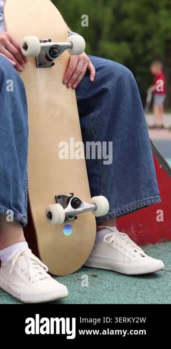 Close-up of legs in white sneakers and skateboard. Young woman in blue ...
