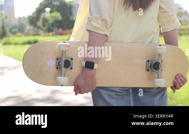 Young woman in yellow shirt and jeans holding skateboard behind her ...