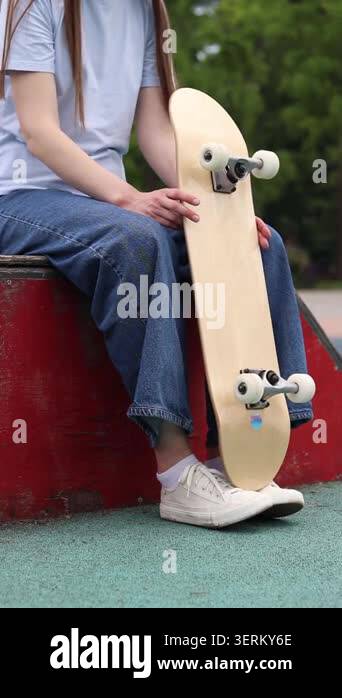 Close-up of legs in white sneakers and skateboard. Young woman in blue ...
