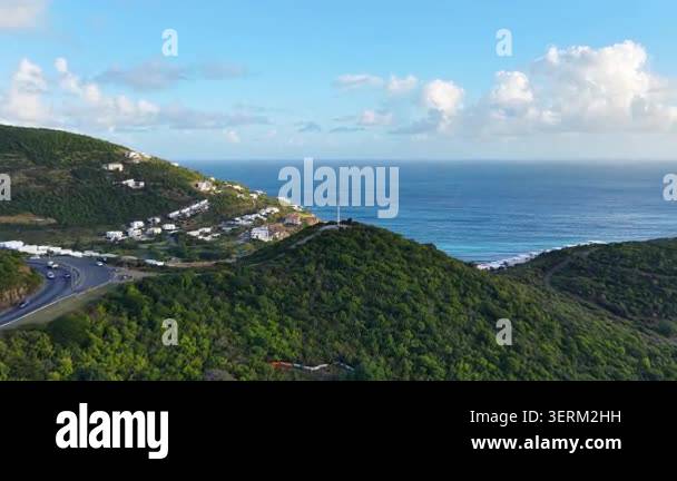 Aerial view of a coastal road winding around green hills in Saint ...