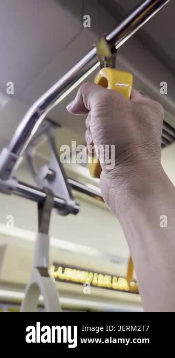 Close-up of a passenger holding a train handrail inside a commuter ...