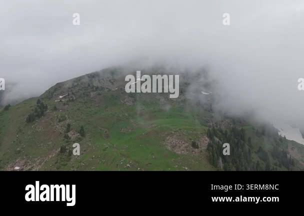 Fog envelops a mountainous landscape, gradually revealing green hills ...