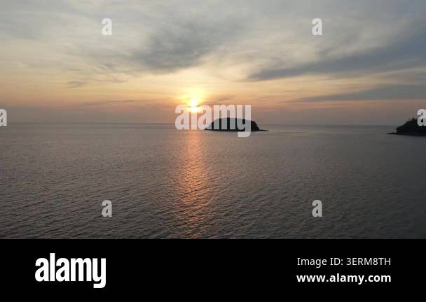 The sun sets over tranquil ocean waters, casting golden reflections on ...