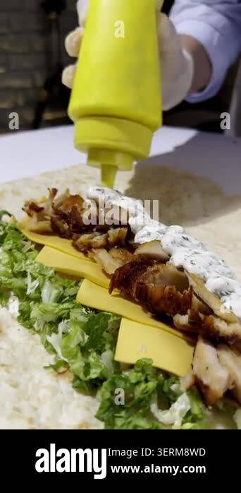 Close up of chef hands adding sauce onto an open tortilla wrap with ...