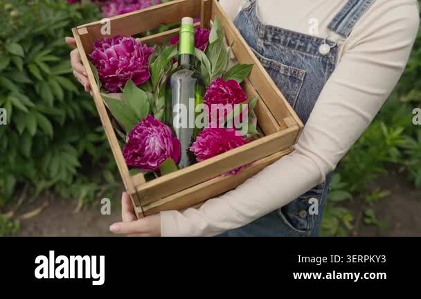 Woman in work overalls holding a wine bottle among blooming flowers in ...