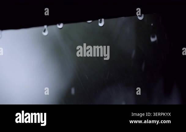Rainwater dripping from roof edge during powerful thunderstorm. Dark ...