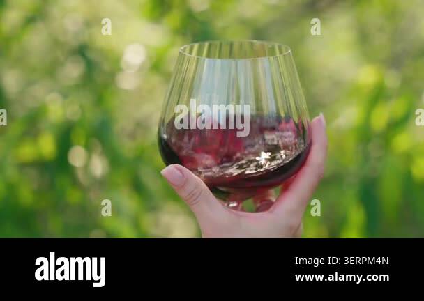 Close-up of red wine moving inside a large stemmed glass held outdoors ...