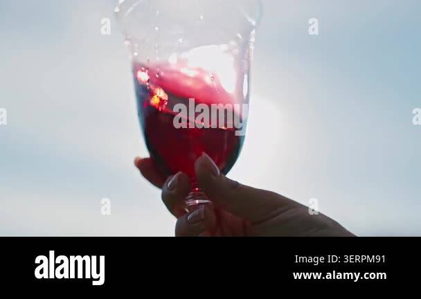 Glass of red wine shines against the sky with colorful light ...