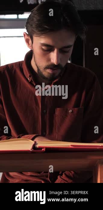 Front view of man sitting in mosque reading Islamic Quran book at table ...