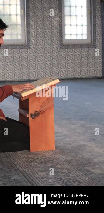 Side view of a bearded man sitting in a mosque reading the table ...