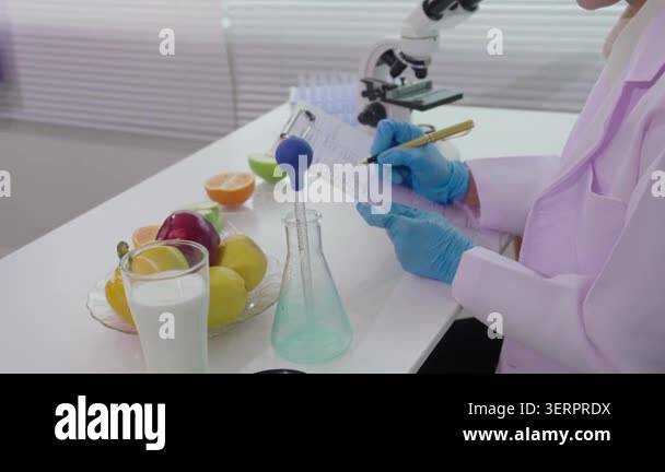 Female food scientist in lab coat looking through microscope, analyzing ...