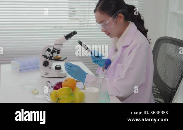 Female food scientist in lab coat looking through microscope, analyzing ...