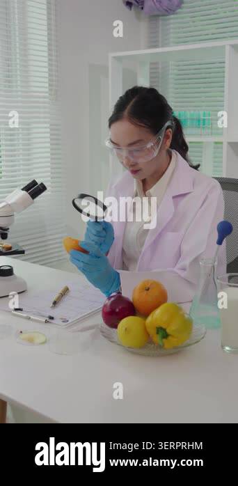 Female food scientist in lab coat looking through microscope, analyzing ...