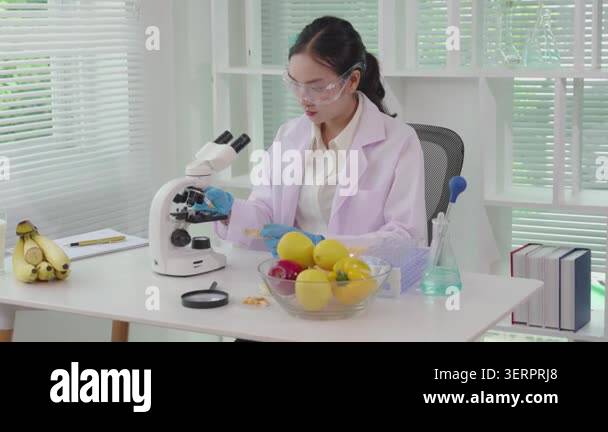 Female food scientist in lab coat looking through microscope, analyzing ...