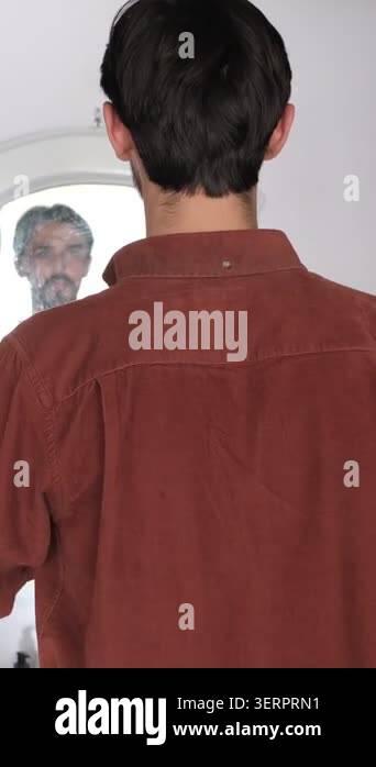 Young caucasian bearded man wearing his shirt in front of the mirror at ...