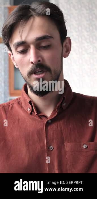 Front view of a bearded young man sitting with raised hands praying ...