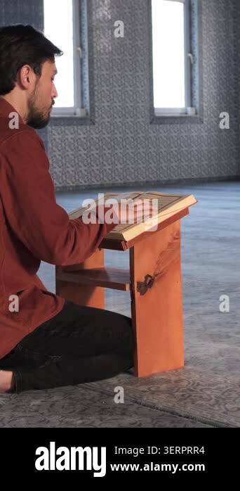 Side view of a bearded man sitting in the mosque on a table reading the ...
