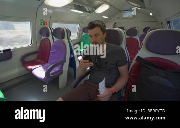 Young man traveling on an empty Italian train with colorful seats using ...