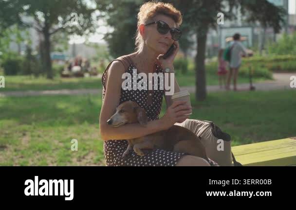 Elderly woman drinking coffee to go sitting on bench holding dachshund ...