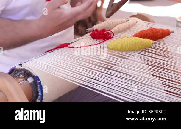 Colored yarn spools are prepared and positioned on a wooden loom during ...