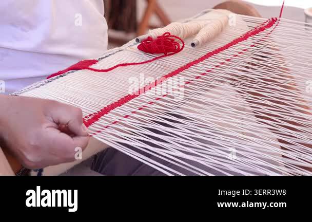 A handloom weaver packs threads tightly together using a wooden beater ...
