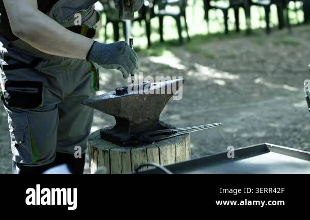 A blacksmith uses a hammer and punch on metal placed on an anvil during ...