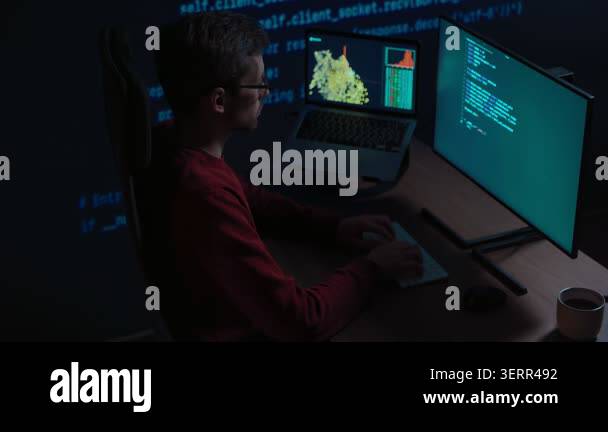 Concentrated data scientist typing code in a dimly lit workspace ...
