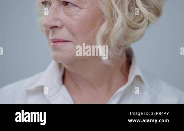 Close-up of charming mature lady with blonde wavy hair in white shirt ...
