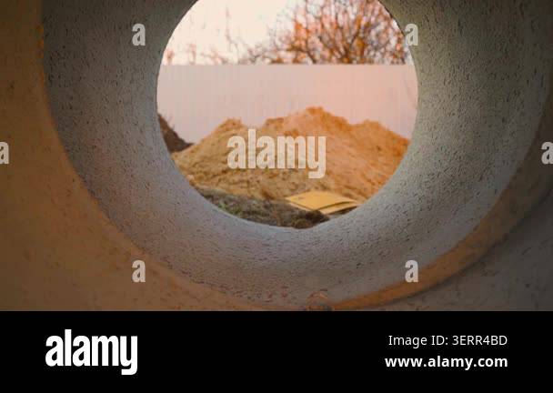 View through concrete sewer pipe ring at sand pile on construction site ...