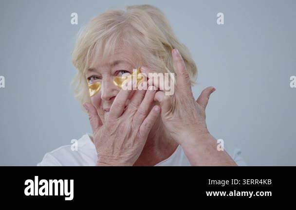 Happy senior woman applying hydrogel eye patches on face in front of a ...