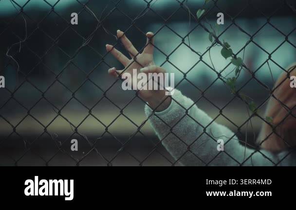 A young woman with short dyed hair stands behind a chain-link fence ...