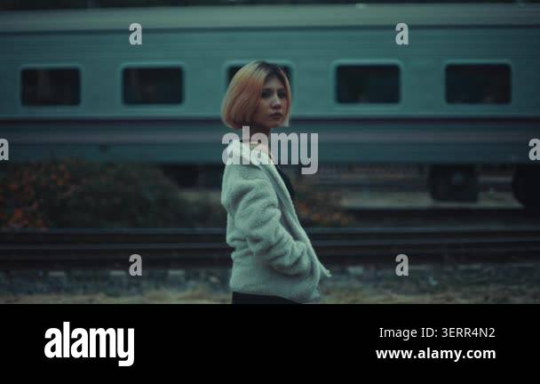 Young blonde woman in a light fleece jacket stands on a gravel train ...