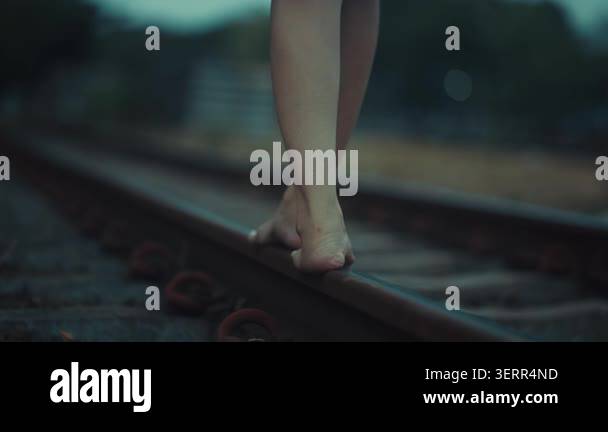 Back view of a young barefoot girl carrying shoes in her right hand as ...