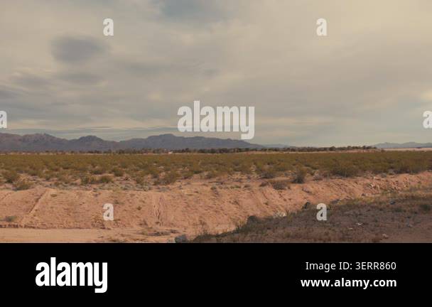 Arid desert landscape with dry bushes and distant mountains under a ...