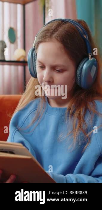 Happy preteen girl in headphones reading interesting book, turning ...