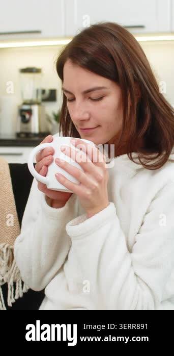 Young woman at home makes herbal tea holds warm cup takes slow sip and ...