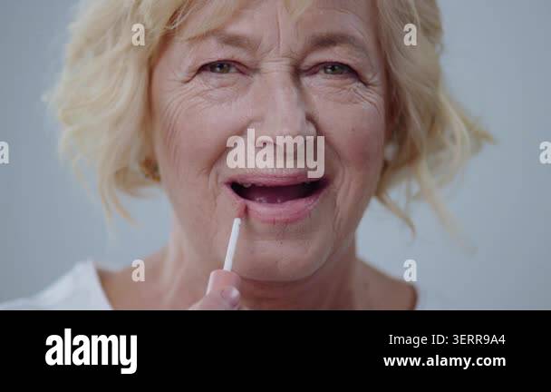 Close-up of beautiful grandmother applying lip gloss on lips preparing ...
