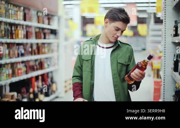 Young smile man choose alcohol in supermarket with shopping cart wine ...