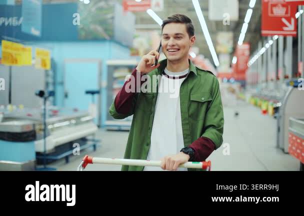 Handsome man walk in supermarket speak on phone smiling feel happy ...