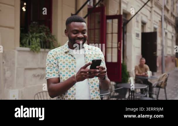 Handsome African guy with beard standing in the street with smartphone ...