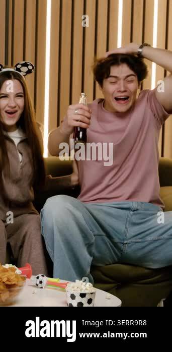 Young Asian man and woman share a joyful moment on a couch, raising ...