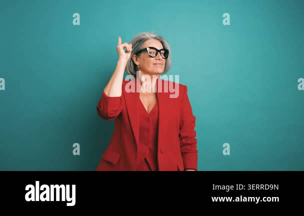 Cheerful mature woman with grey hair and glasses, wearing a vibrant red ...