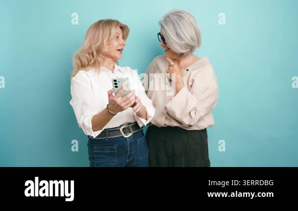 Two stylish senior friends having fun while using a smartphone. The ...