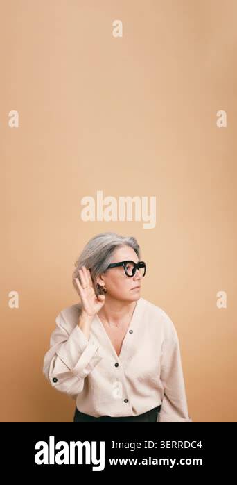 Expressive elderly woman with grey hair and glasses cupping her ear ...