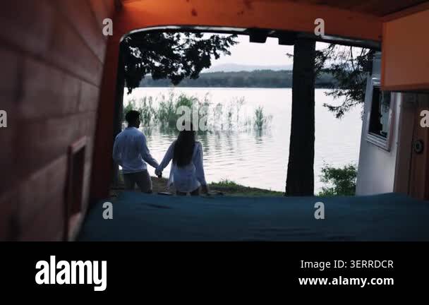 Young romantic couple holding hands and watching the sunset over a lake ...