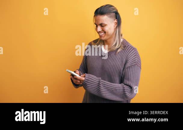 Cheerful young man with long hair smiling and texting on his mobile ...