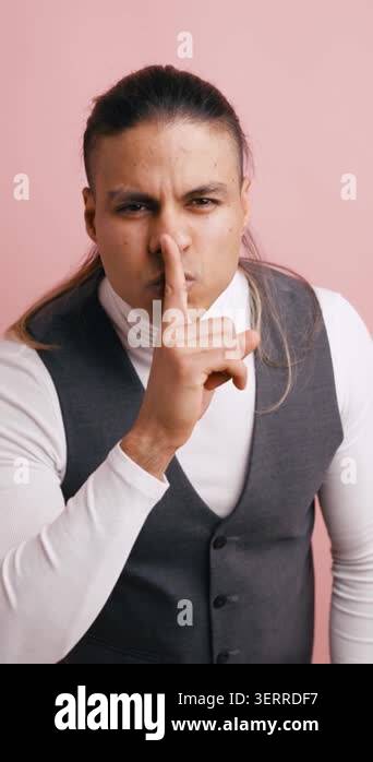 Young latino man with long hair making a shushing gesture with his ...