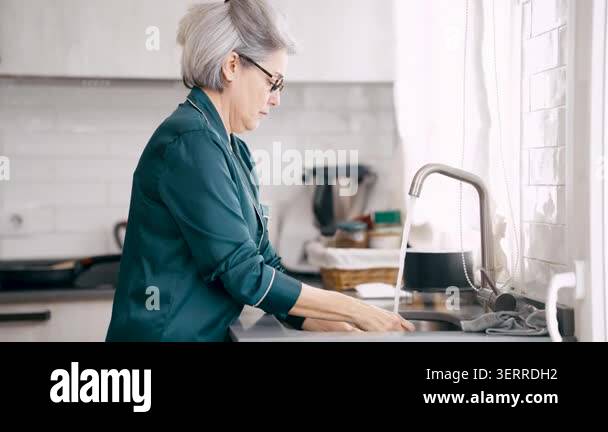 Elderly woman in pajamas doing daily chores in her modern kitchen ...