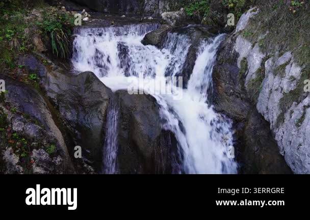 Water flows over rocks in a small waterfall, moving downward through a ...